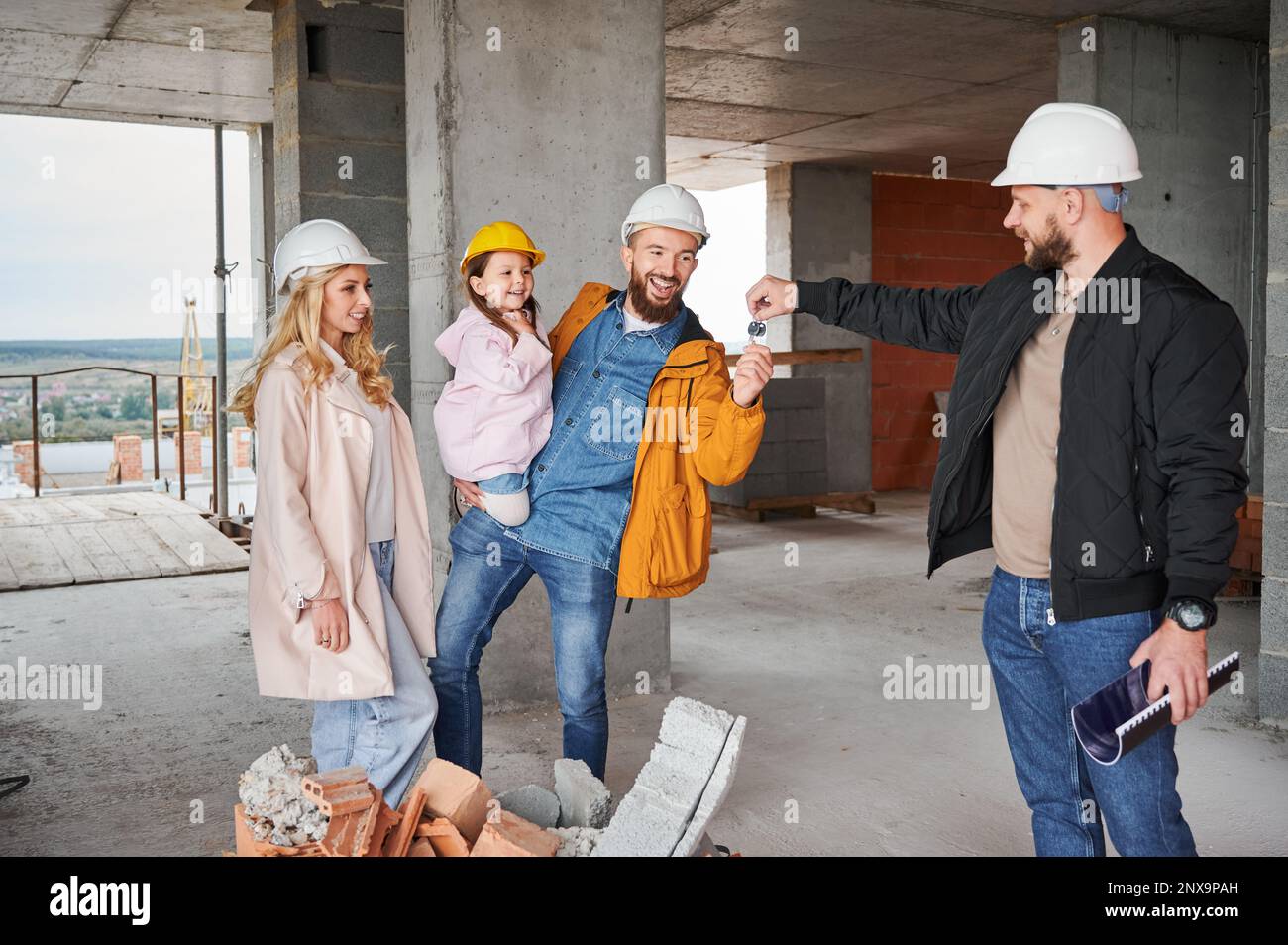 Male builder handing keys from new apartment to family with child at ...