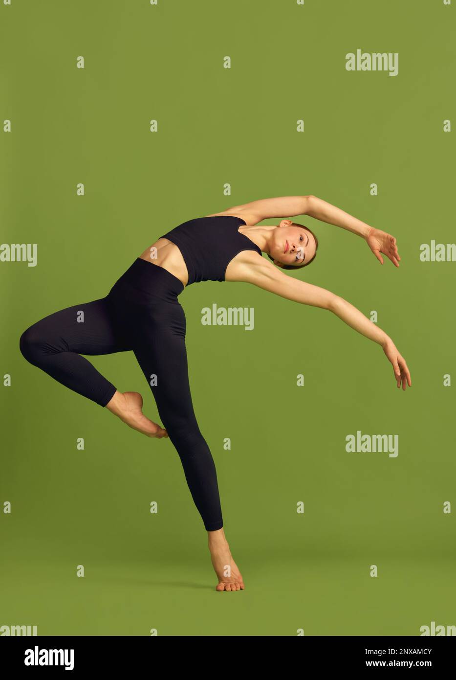 Graceful movements. Young girl doing stretching, training over green ...