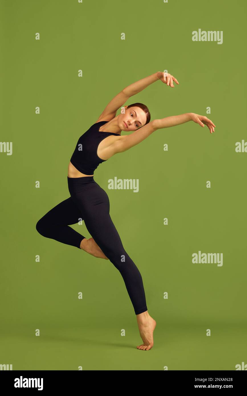 Graceful movements. Young girl doing stretching, training over green ...