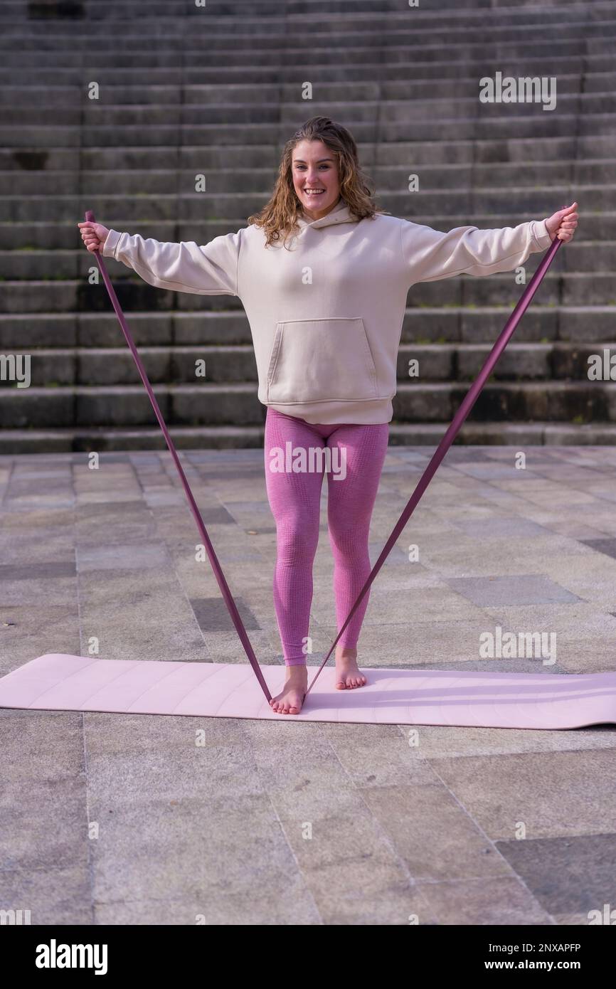 A vertical shot of a young caucasian woman exercising with a resistant ...