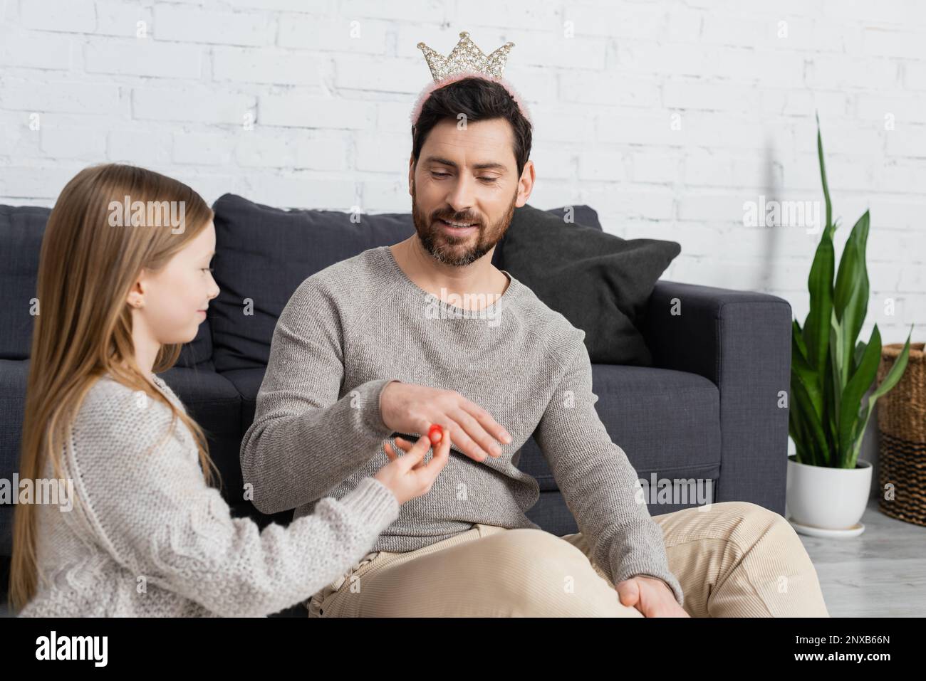 happy girl wearing toy ring on finger of father in crown while playing ...