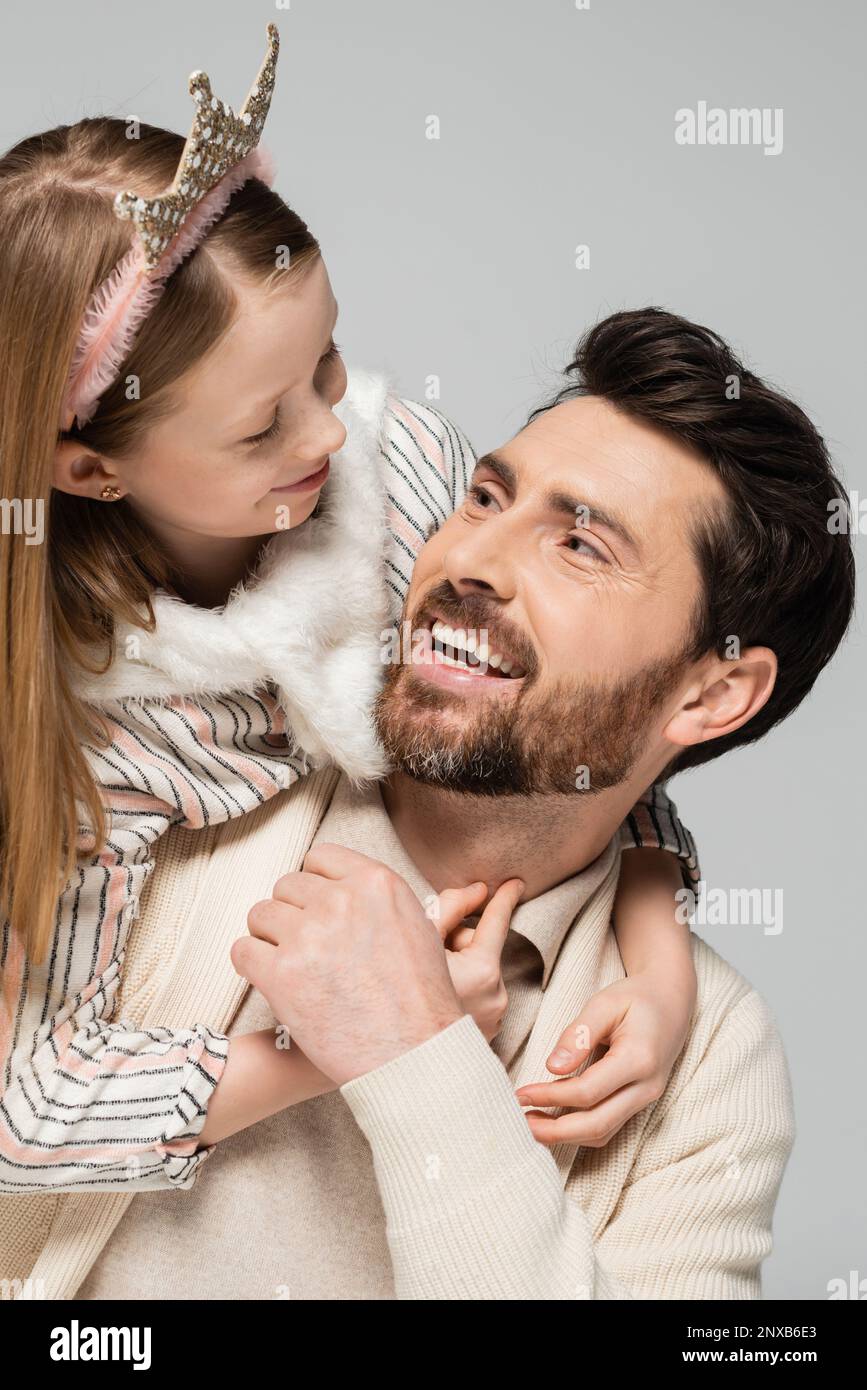 happy kid in crown hugging positive father with beard isolated on grey ...
