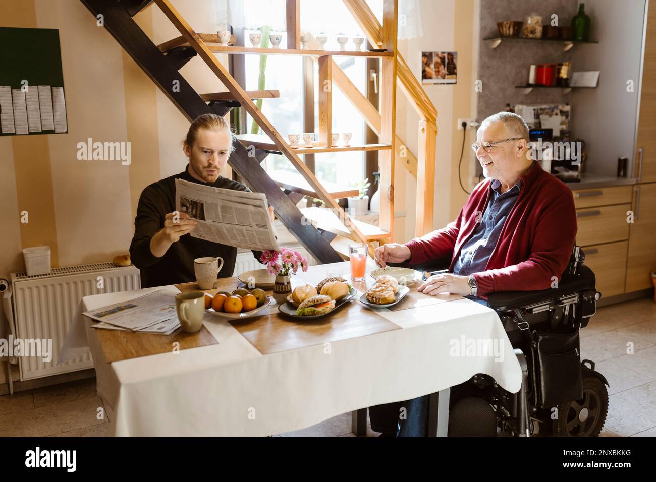 Young man showing newspaper to retired senior father with disability ...