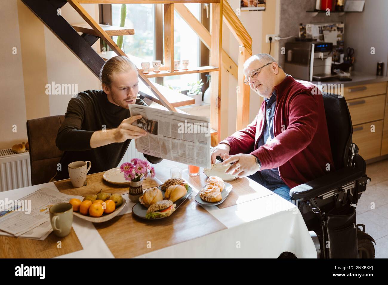 Young man showing newspaper to senior father with disability while ...