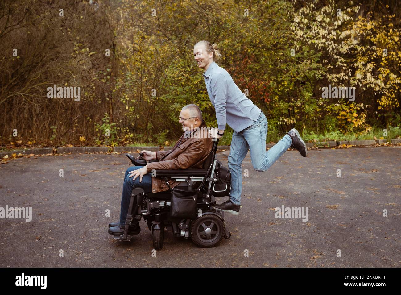 Cheerful young man riding on motorized wheelchair of retired senior ...
