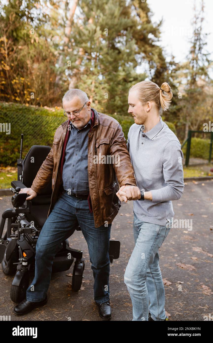 Young male caretaker holding hand of retired senior man with disability ...