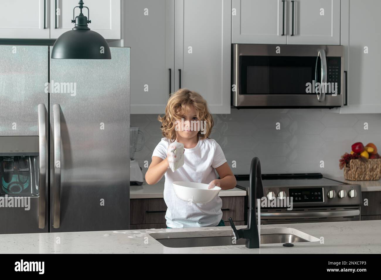 Home chores. Kid in kitchen cleaning plates. Cute boy washing dishes in ...