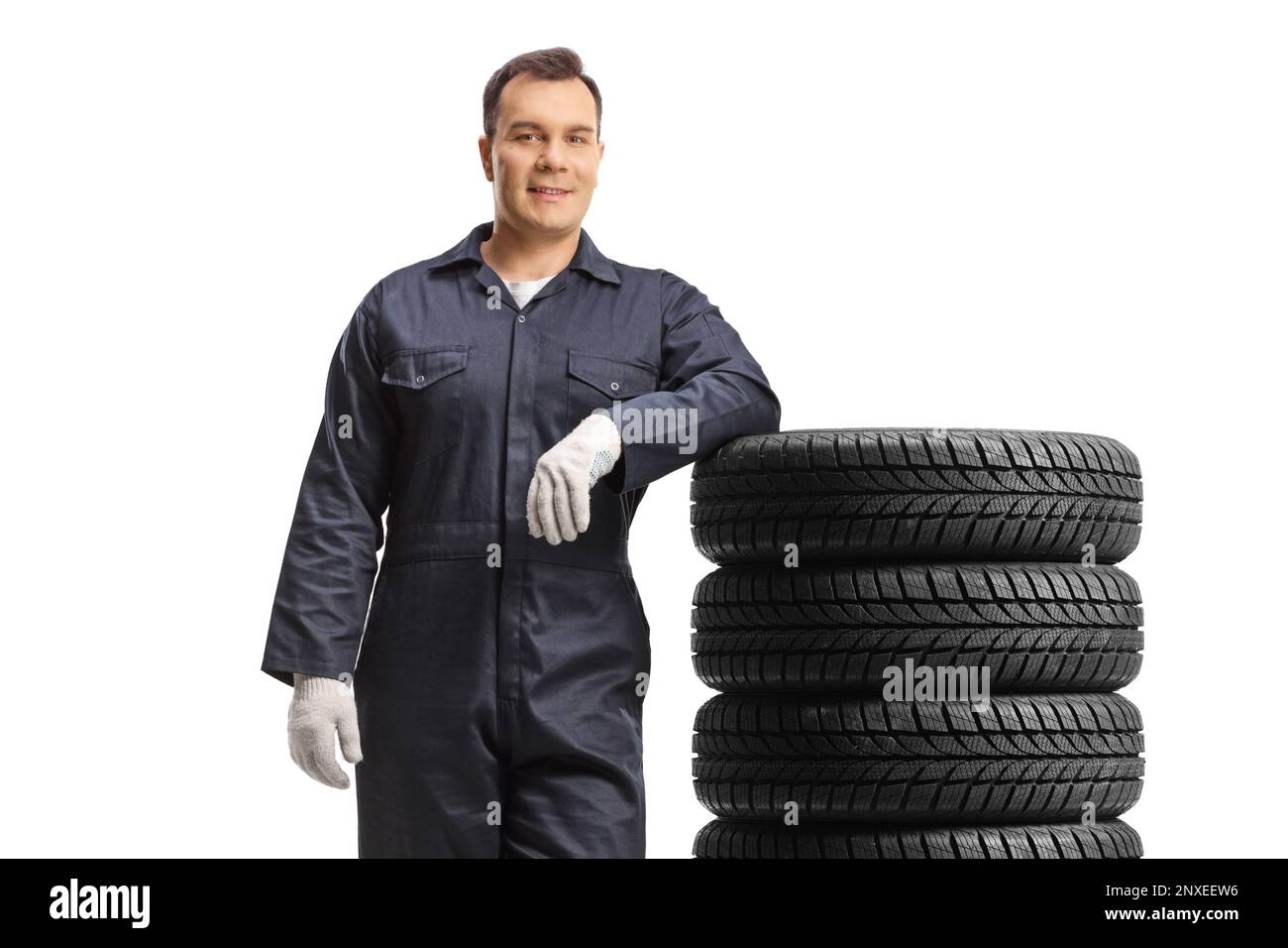 Auto mechanic in a uniform standing and leaning on a pile of tires ...