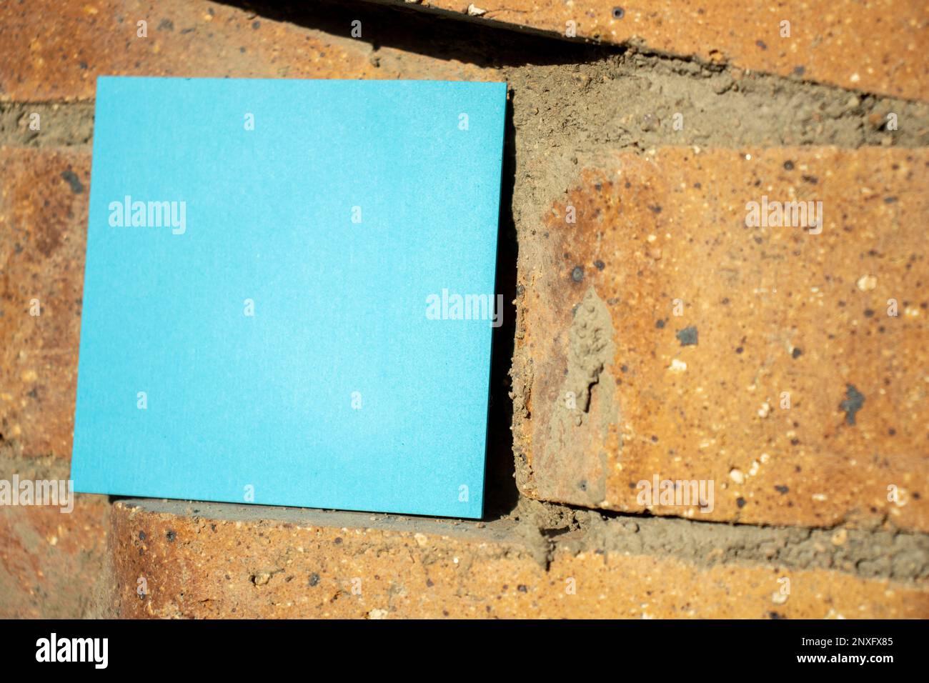 blue square paper note resting on a brick wall in full sun with empty ...