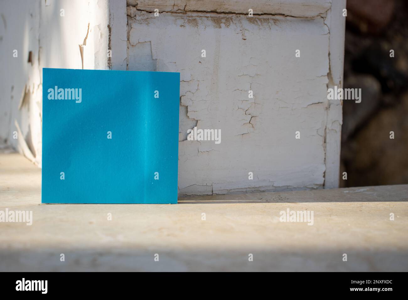 blue square paper note resting on old peeling white paint with empty ...