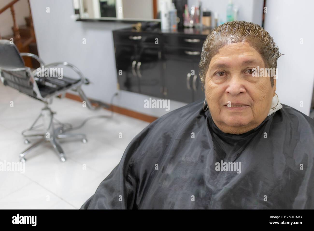 Old woman with dye on her head sitting on a chair in beauty salon with ...