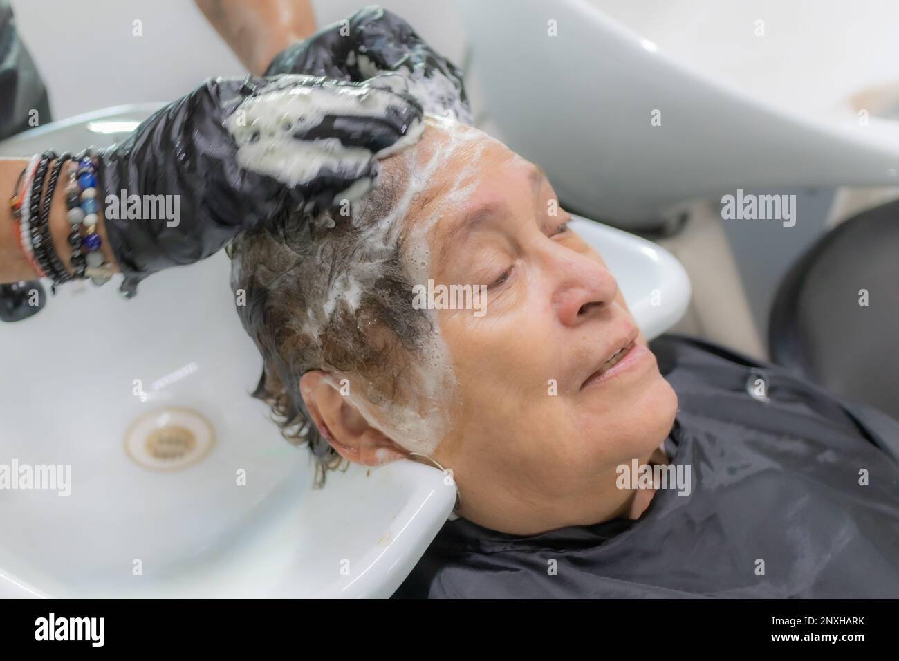Hairstylist washing head of an elderly woman lying relaxed on a sink on ...