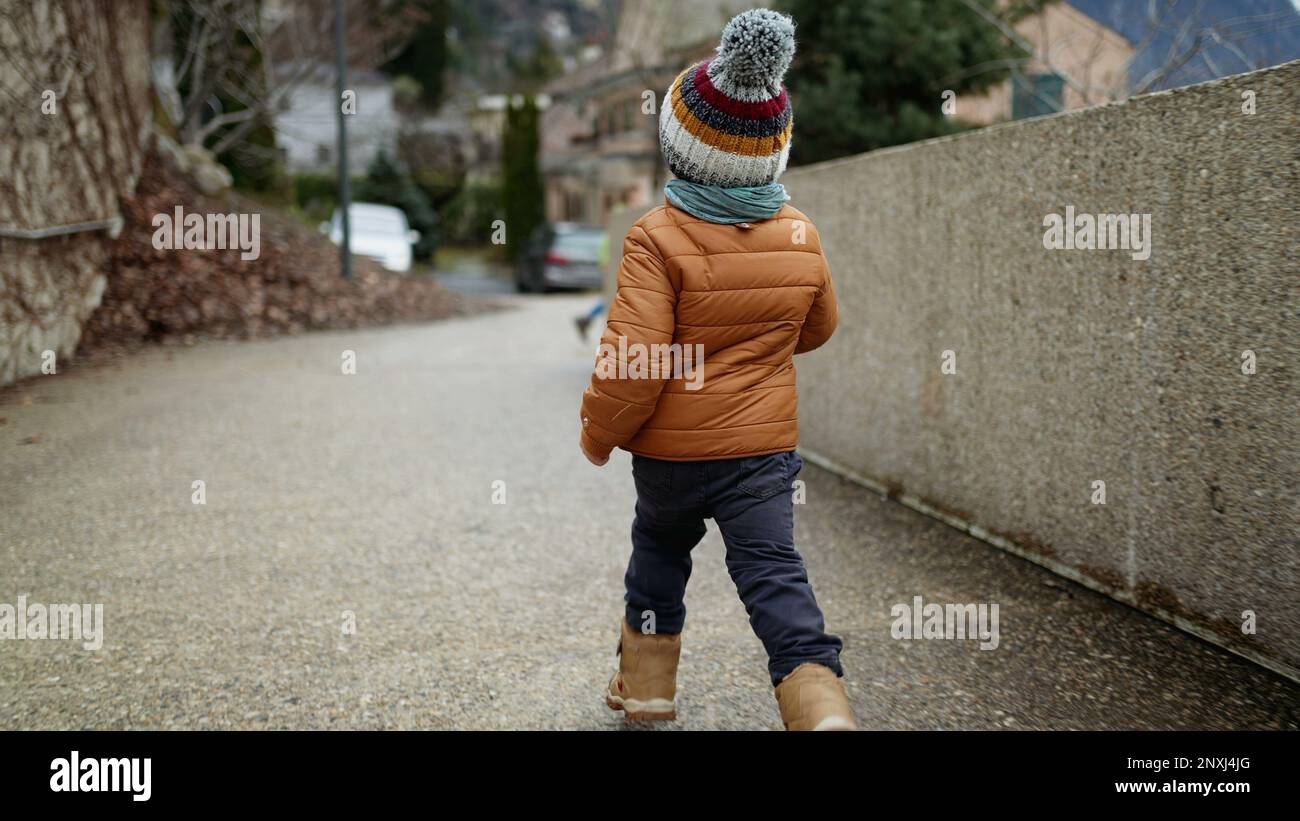 Back of child running outside in urban park corridor wearing winter ...