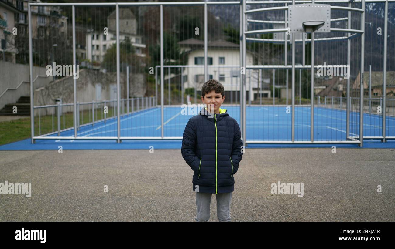 Contemplative young boy standing outside at city park with serious ...