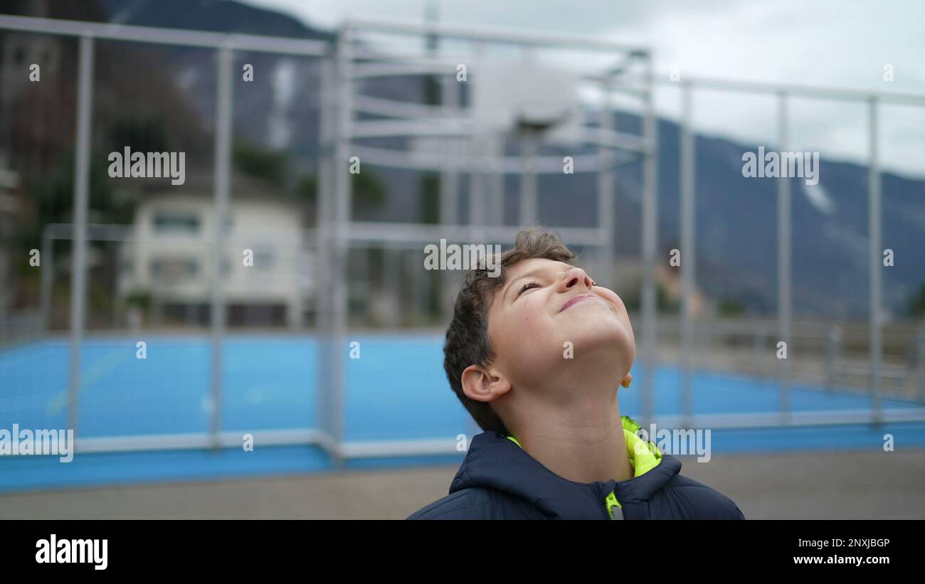 One contemplative young boy looks up at sky. Kid standing outside at ...