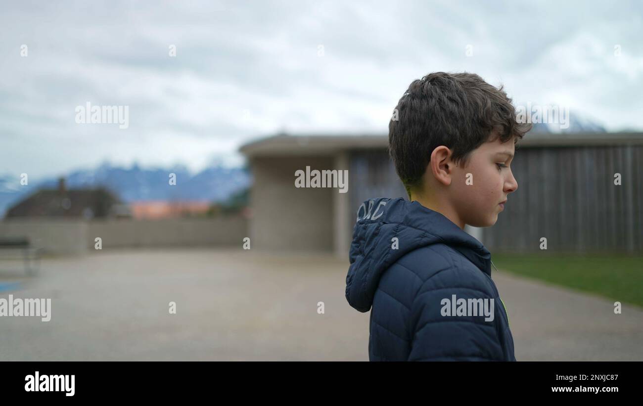 One pensive young boy standing outside thinking. Thoughtful Kid wearing ...