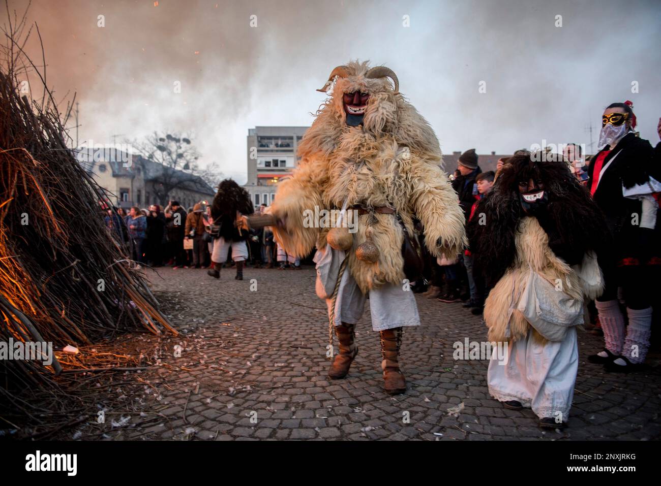 Revellers wearing a sheep wool costume with horns and a mask walk next ...