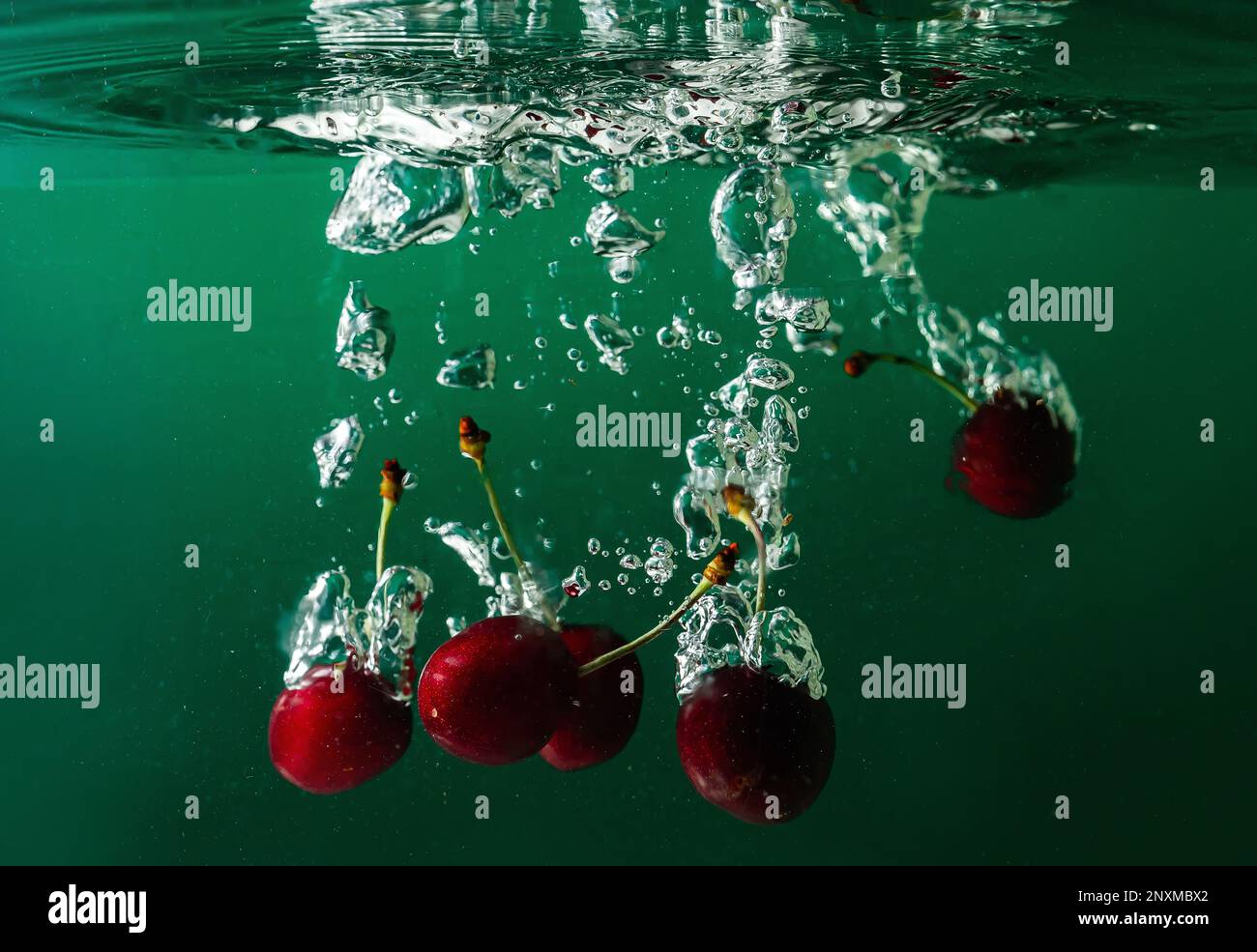 ripe cherries fall into the water raising splashes and air bubbles ...