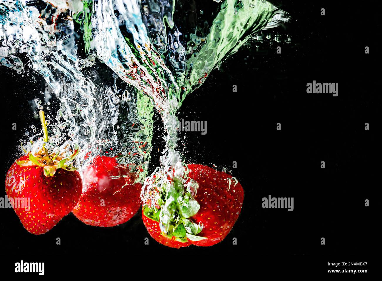 ripe strawberries fall into the water lifting splashes and air bubbles ...