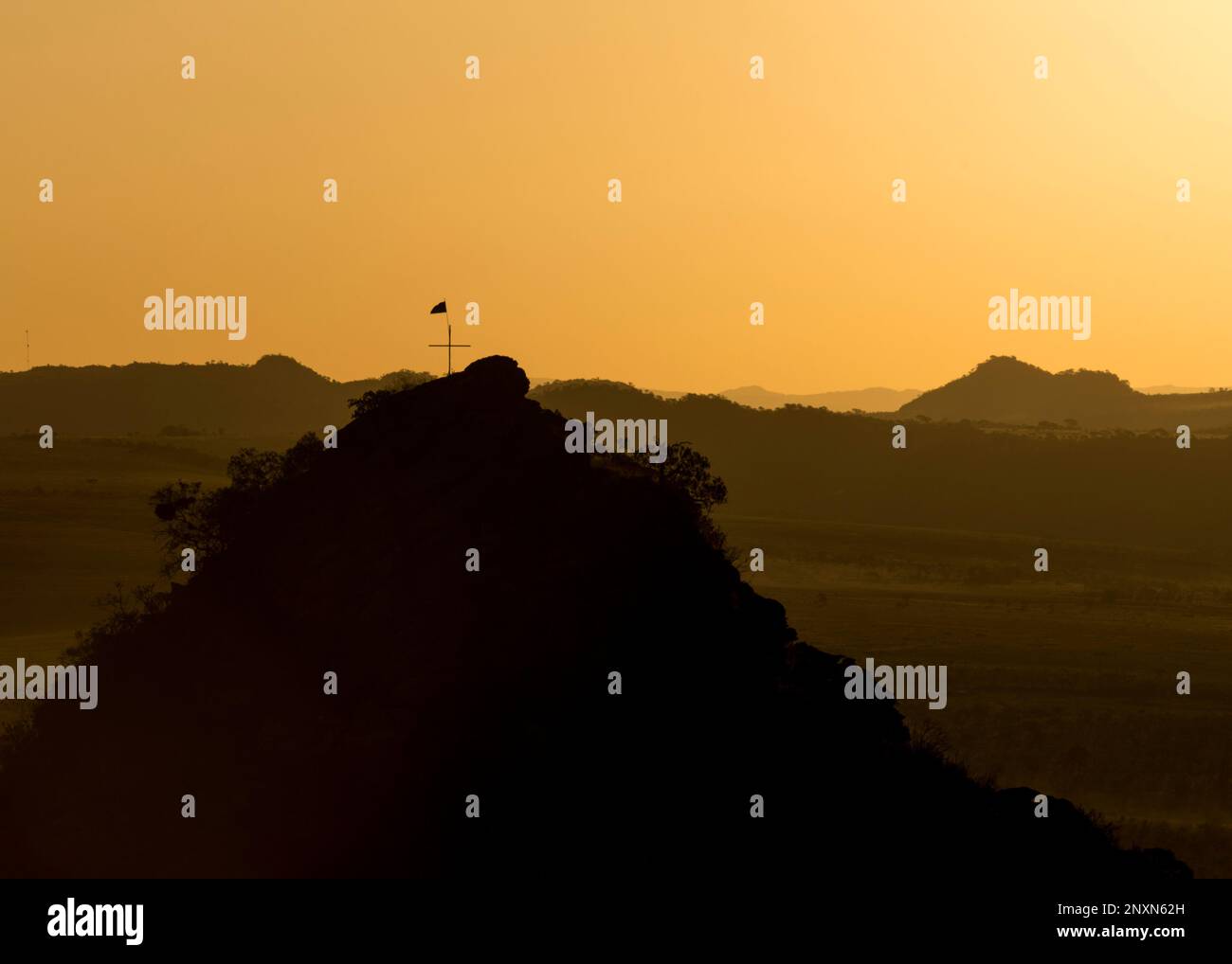 dusk scene overlooking a small mountain peak with cross and flag on top ...