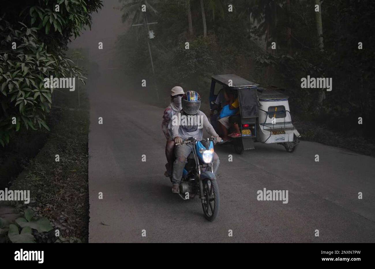 Residents, wearing masks, go on their daily business as Mayon volcano's ...