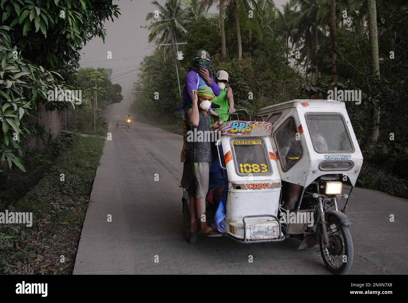 Residents, wearing masks, go on their daily business as Mayon volcano's ...