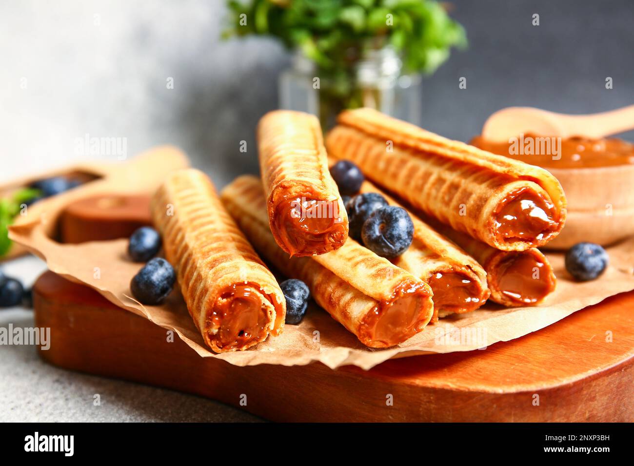 Board of wafer rolls with boiled condensed milk and blueberries on grey ...