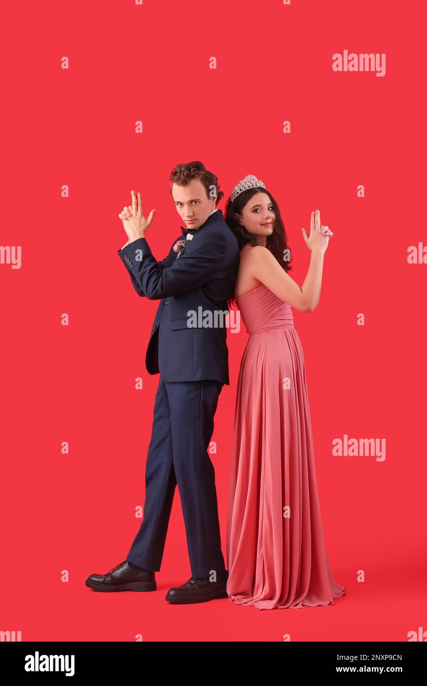Beautiful couple dressed for prom showing gun gesture on red background ...