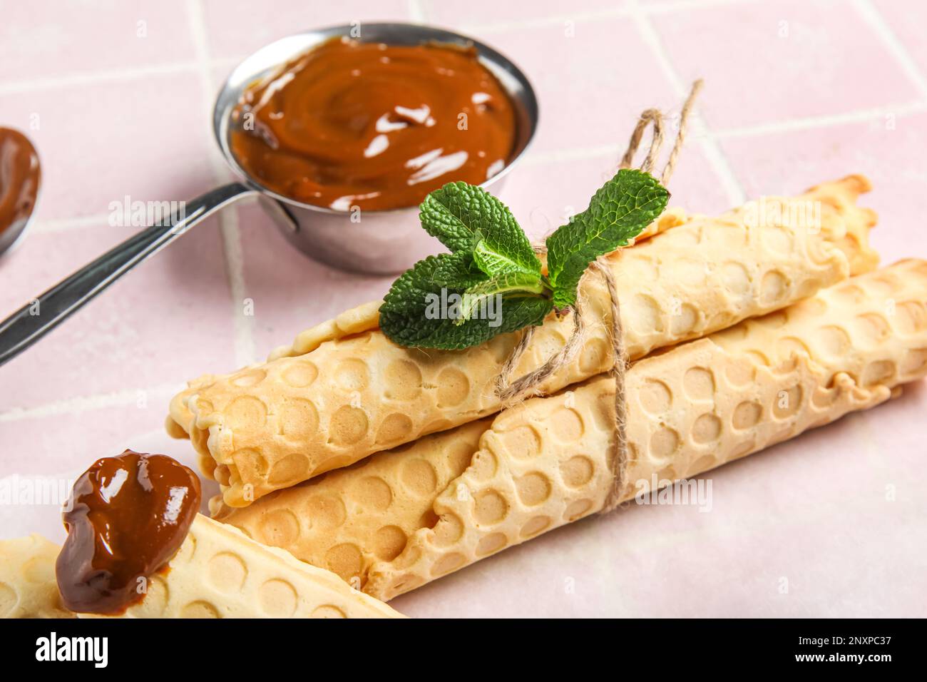 Delicious wafer rolls with mint and boiled condensed milk on pink tile ...