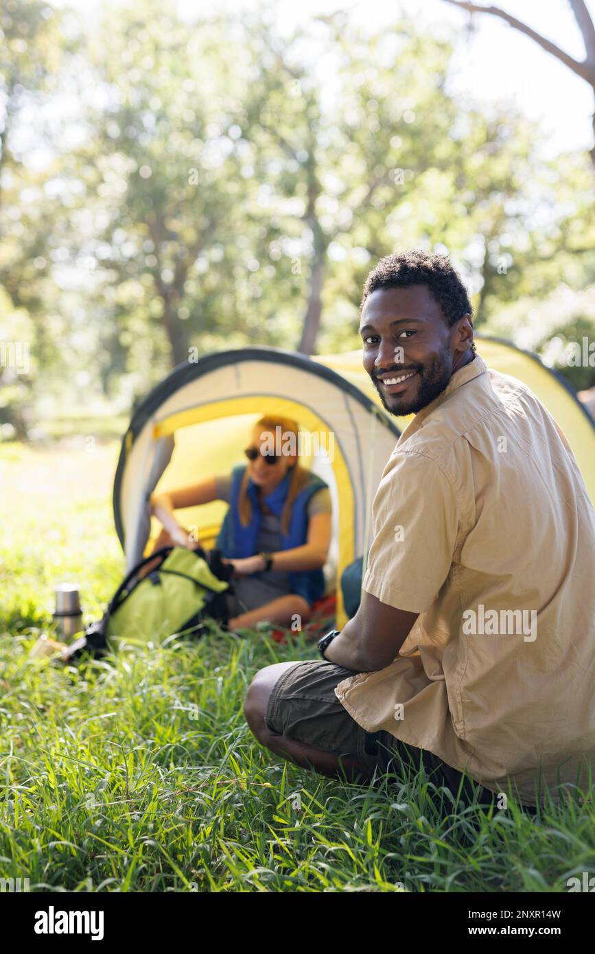 Vertical of happy, diverse couple camping in forest, setting up tent ...