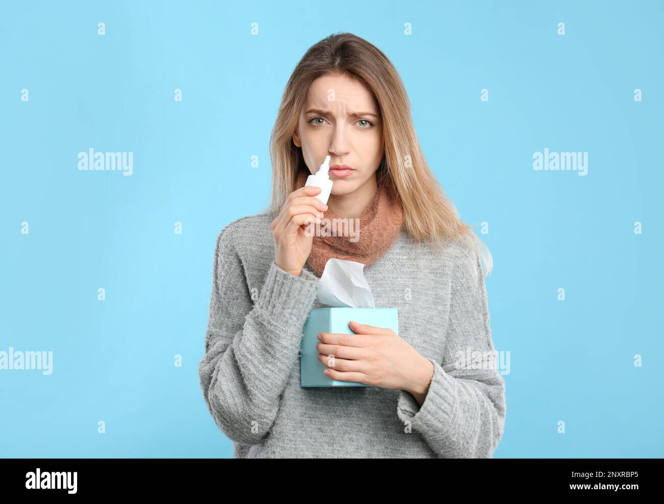 Sick young woman using nasal spray on light blue background Stock Photo ...
