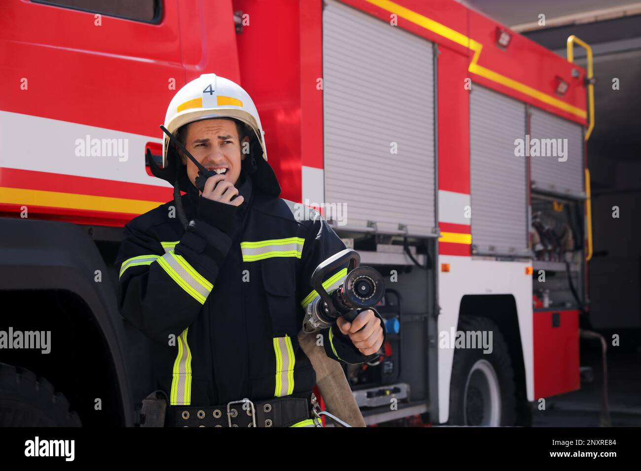 Firefighter in uniform using portable radio set near fire truck ...