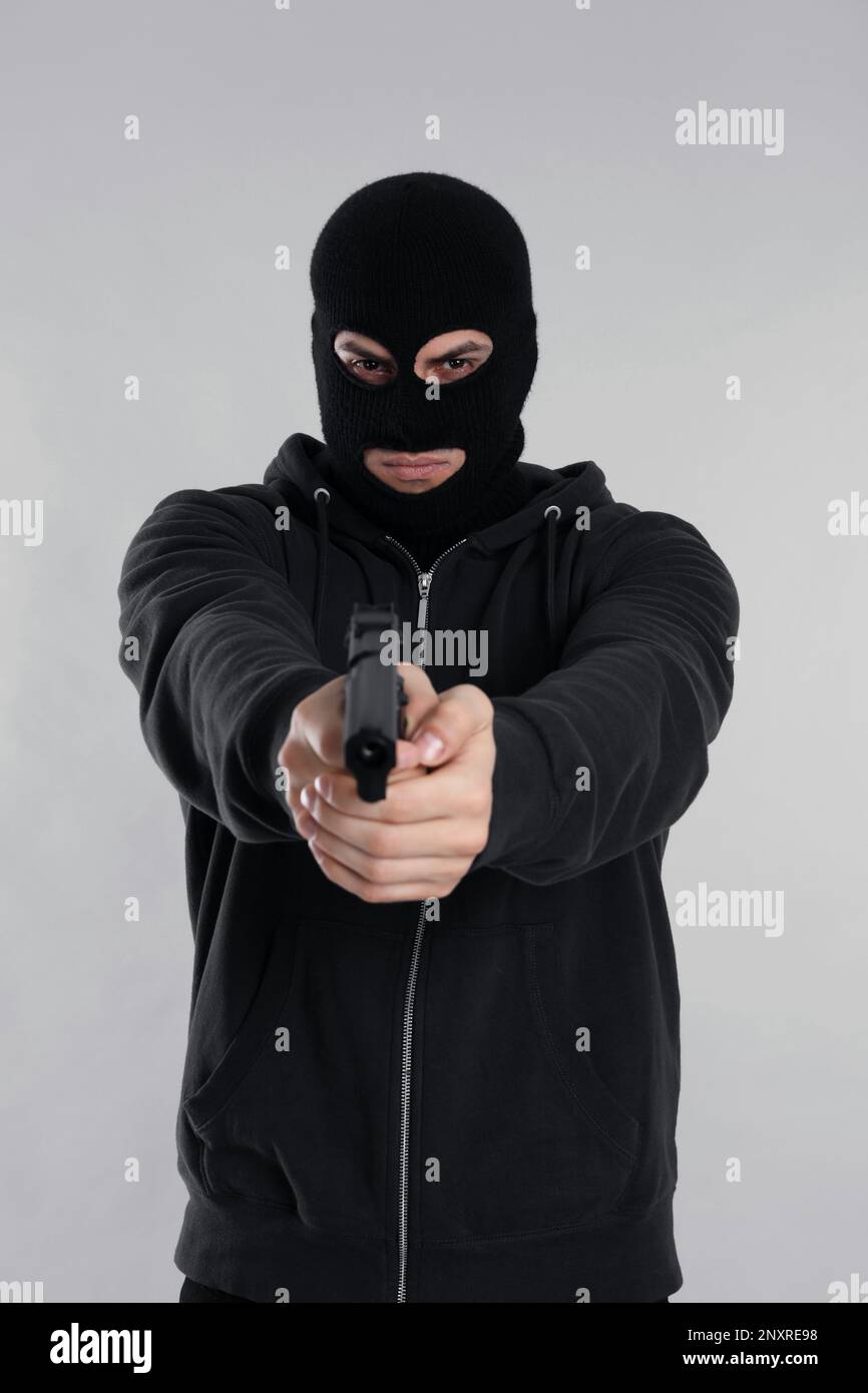 Man wearing black balaclava with gun on light grey background Stock ...