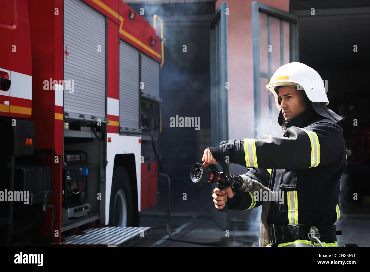 Firefighter in uniform with high pressure water jet near fire truck ...