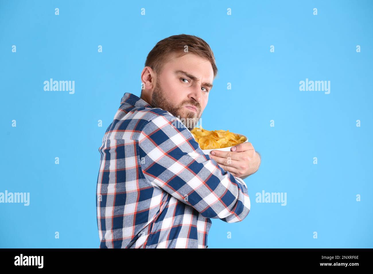 Greedy young man hiding bowl with chips on light blue background Stock ...