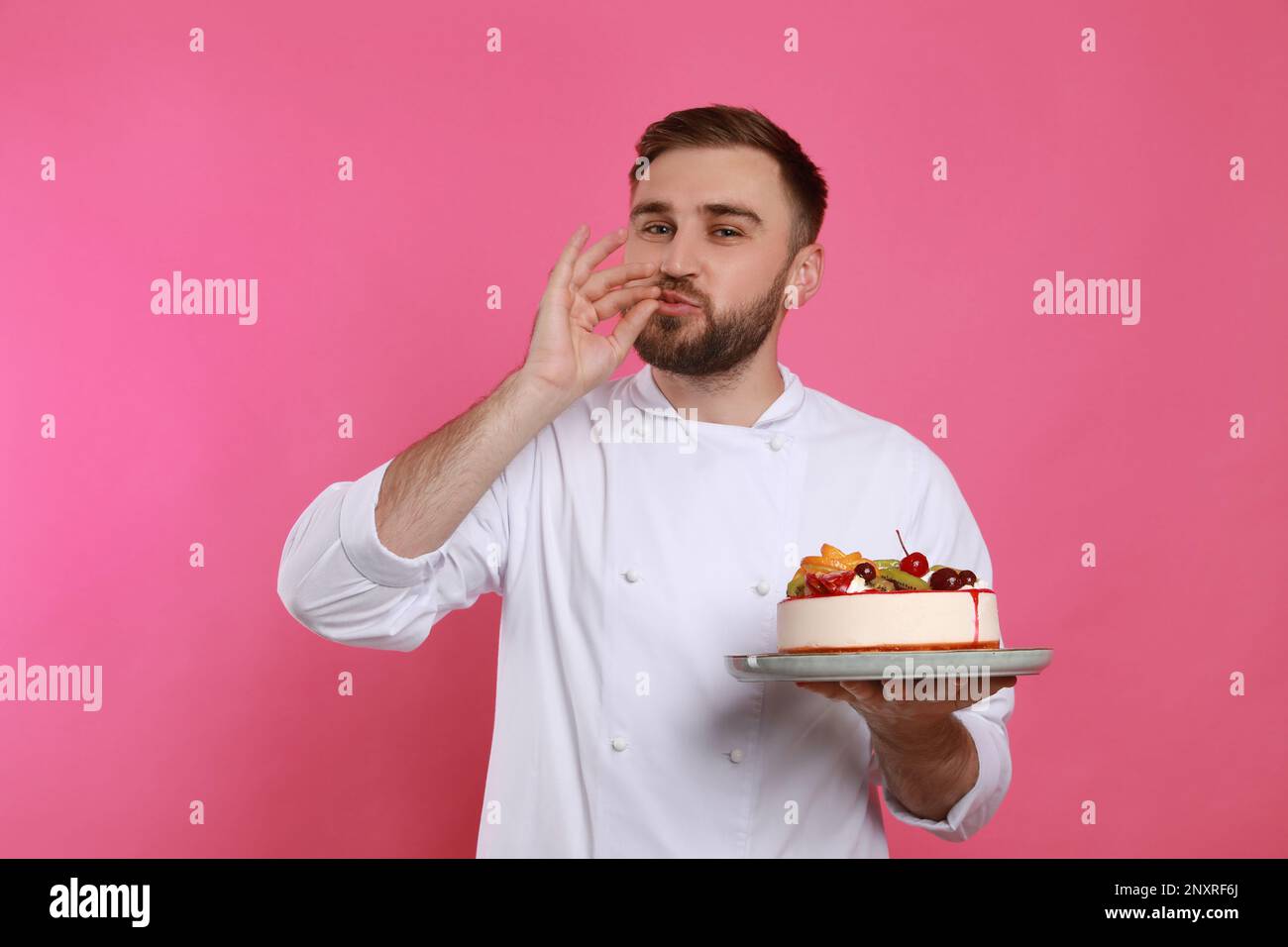 Happy professional confectioner in uniform with cake showing delicious ...