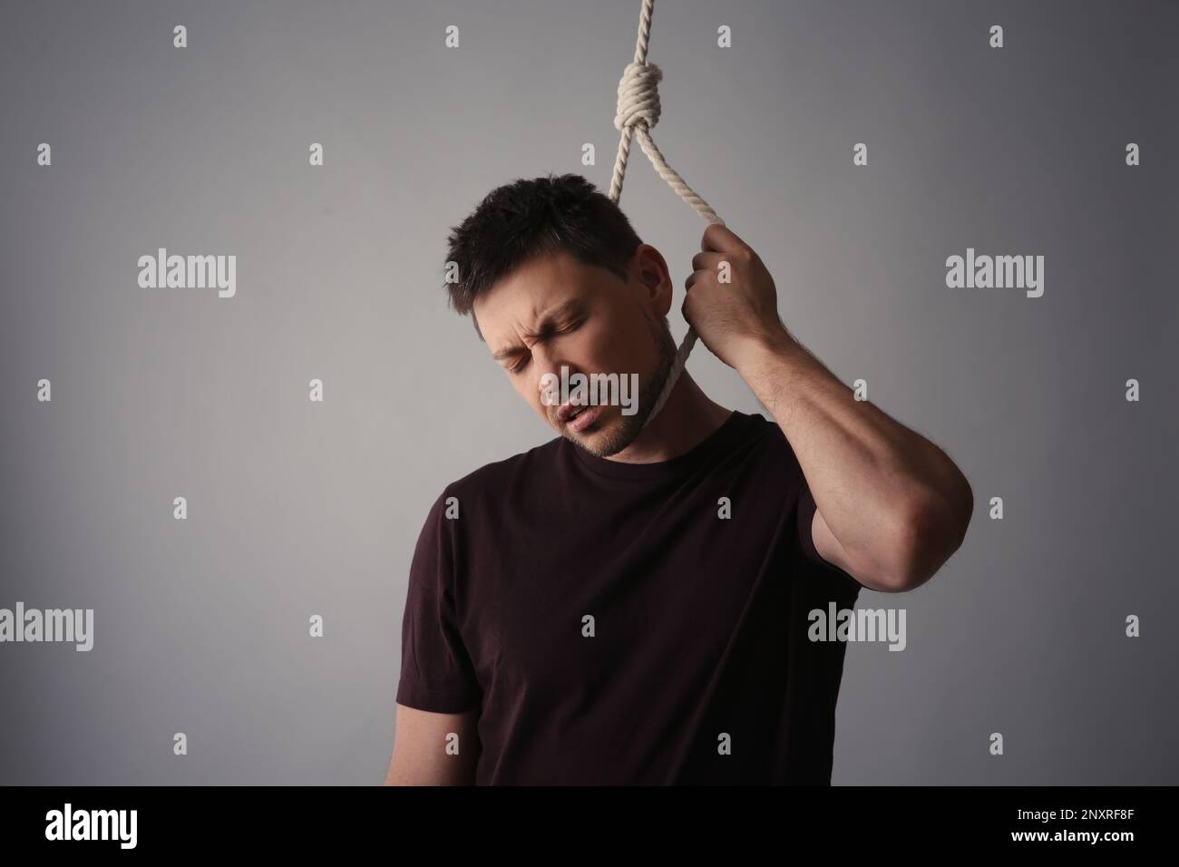 Depressed man with rope noose on neck against light grey background ...