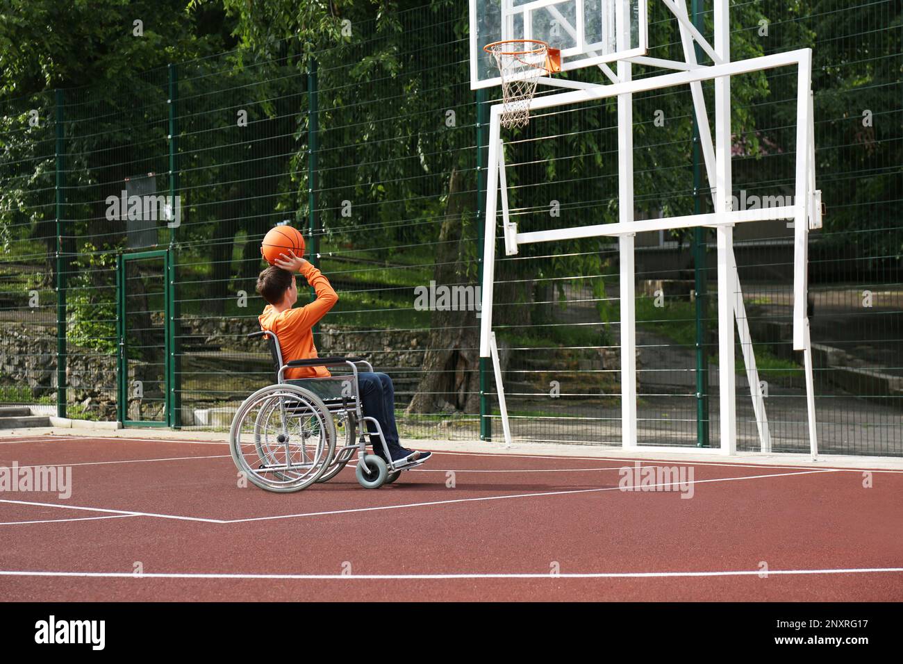 Disabled teenage boy in wheelchair playing basketball on outdoor court ...