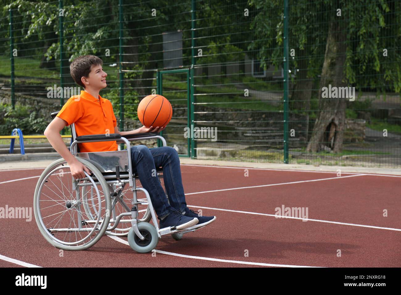 Disabled teenage boy in wheelchair playing basketball on outdoor court ...