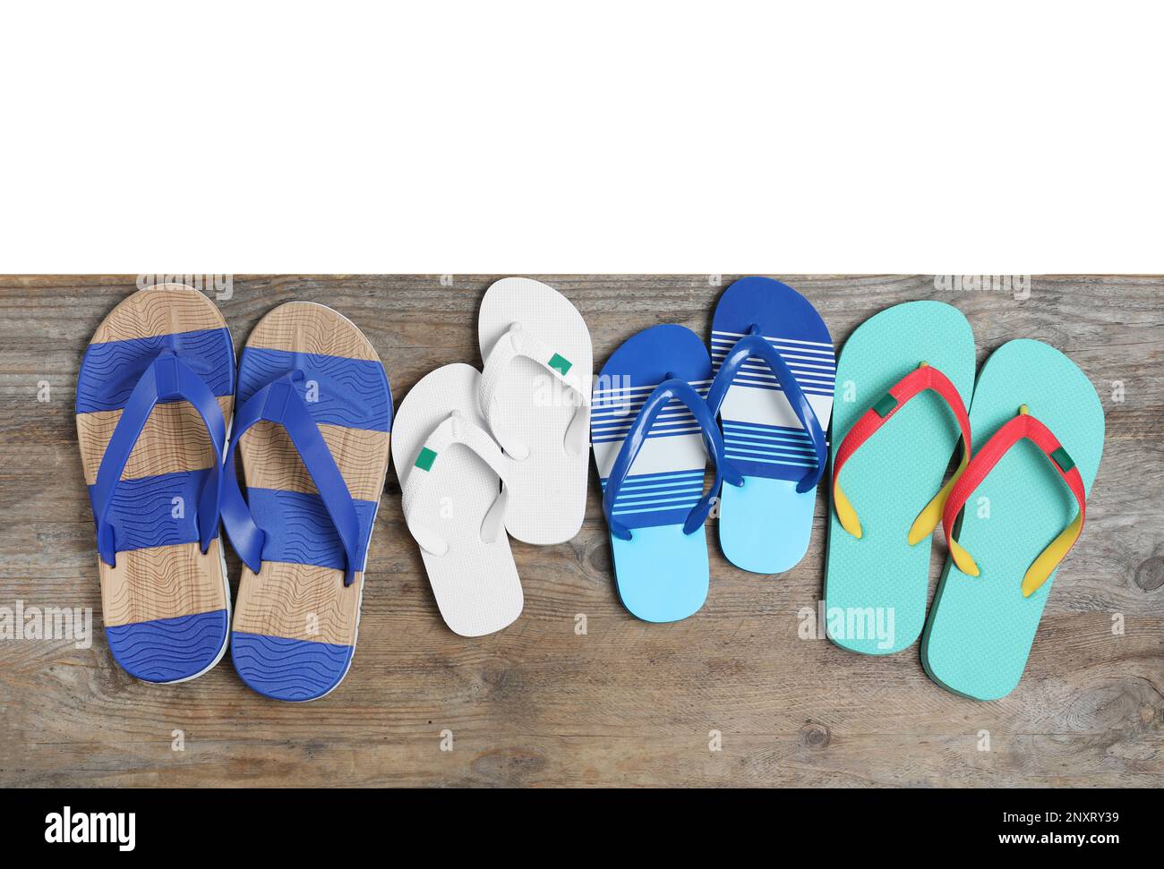 Pairs of bright flip flops on wooden table against white background ...
