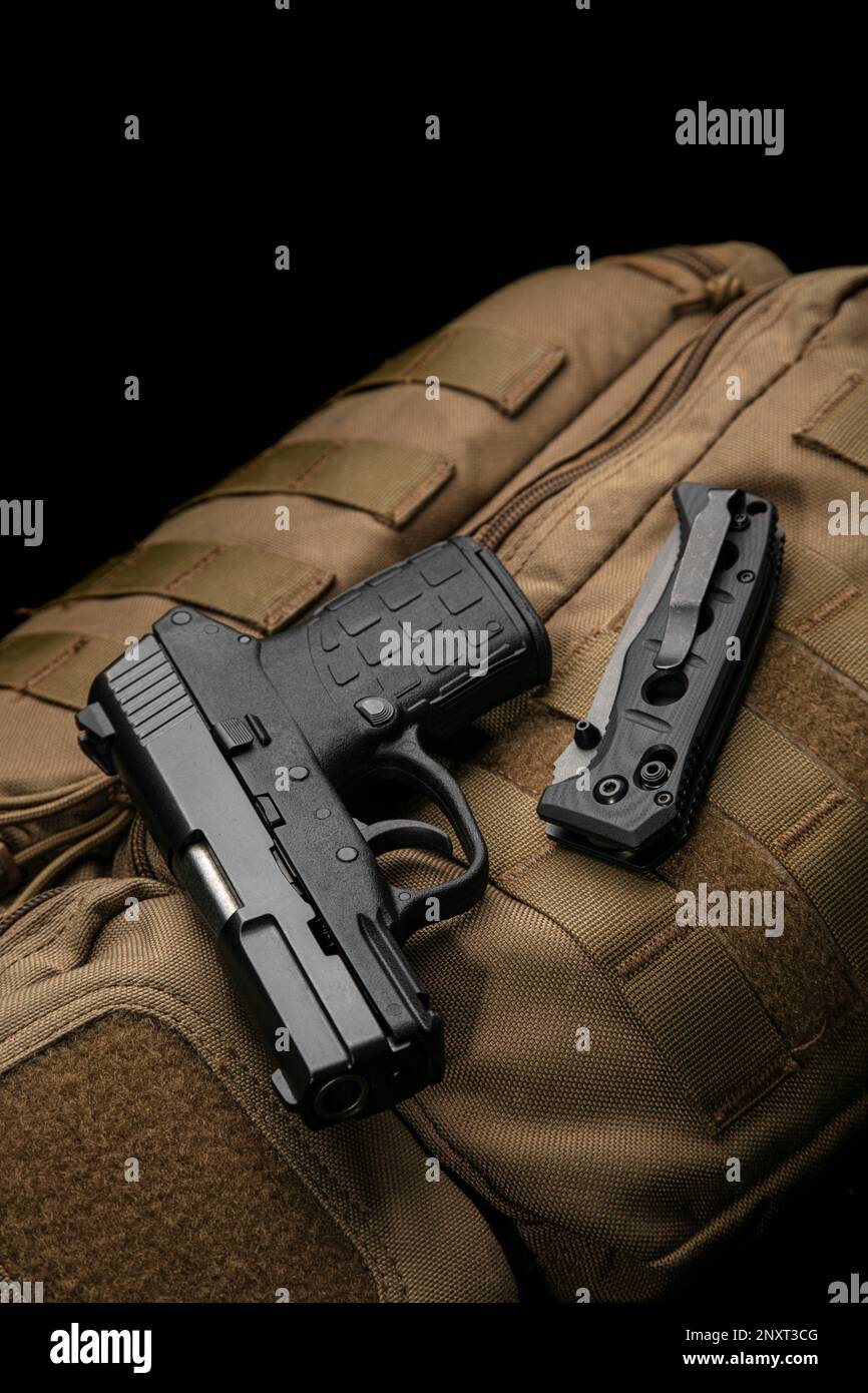 A small modern pistol and penknife on a brown military backpack. Self ...