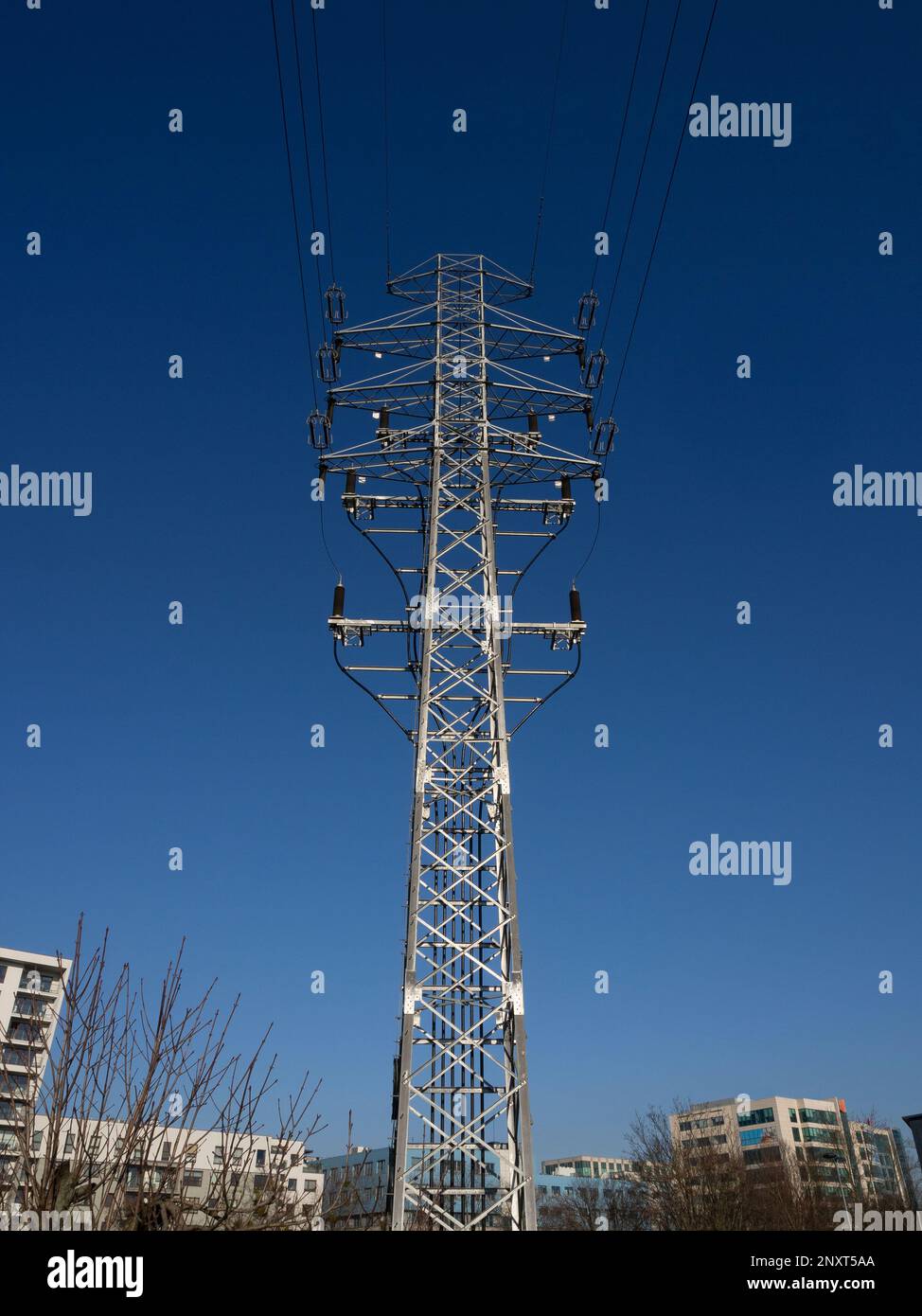 A high-voltage pylon against a blue sky and the buildings of the urban ...