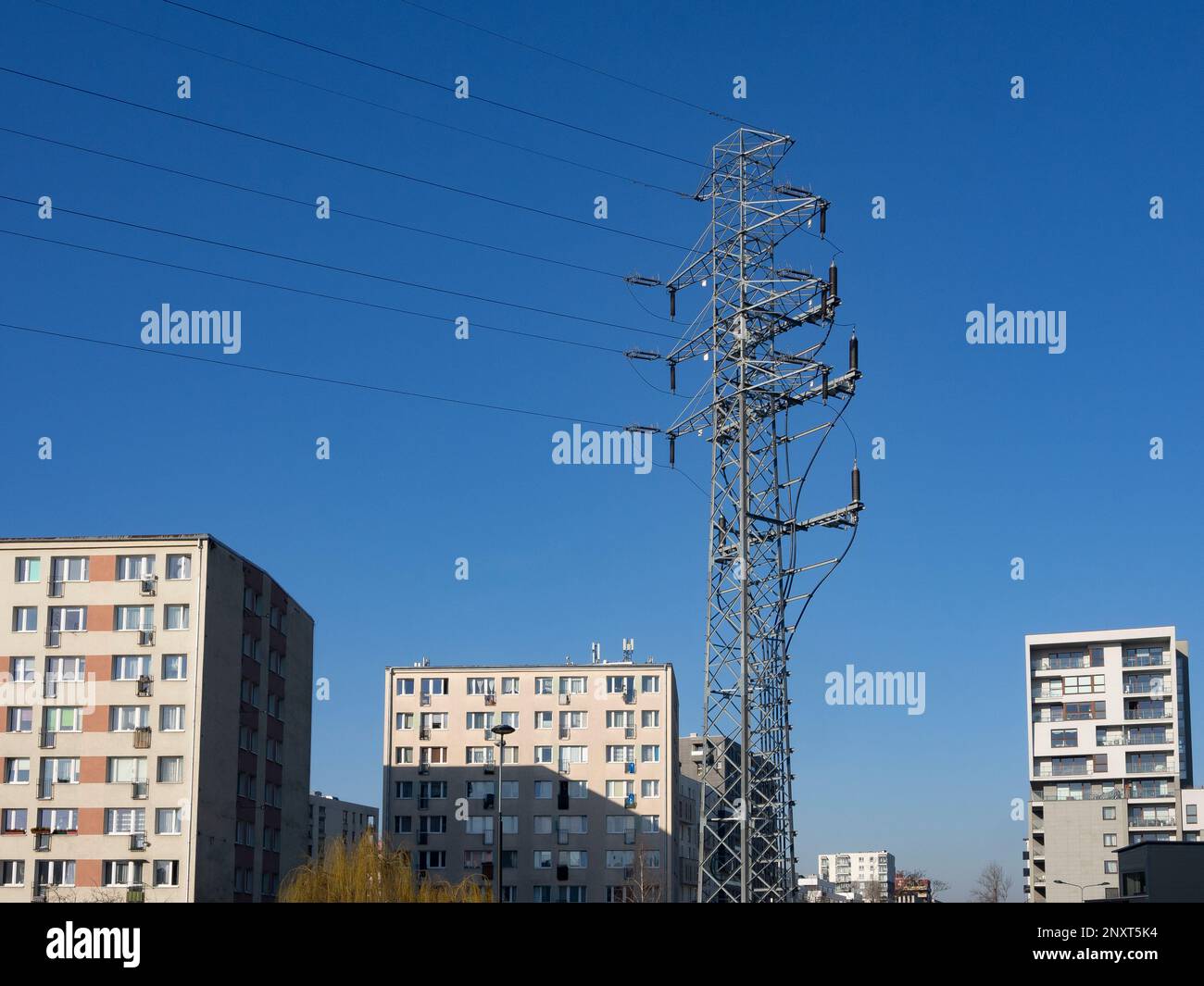 A high-voltage pylon against a blue sky and the buildings of the urban ...