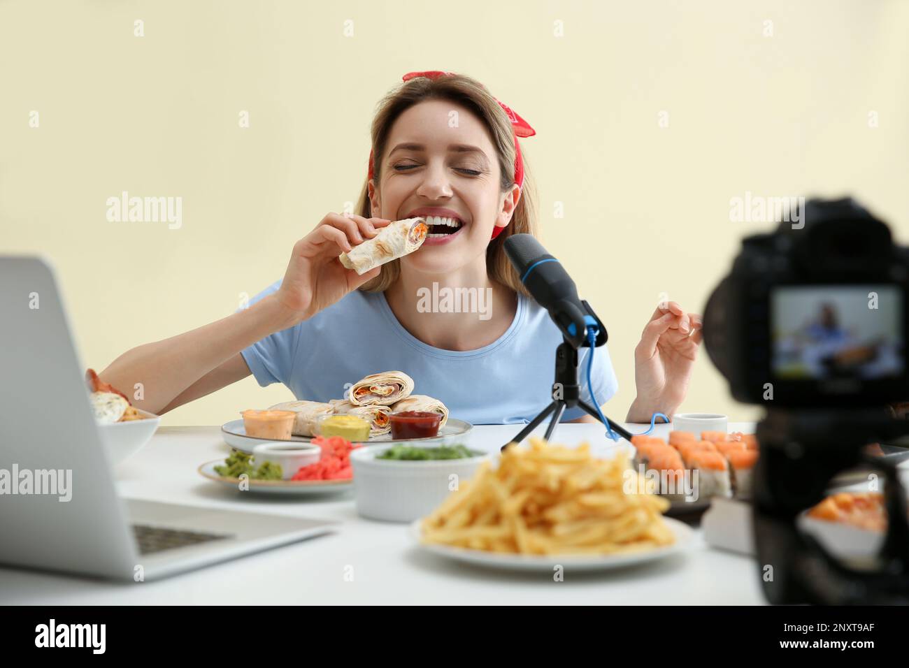Food blogger recording eating show on camera against light background ...