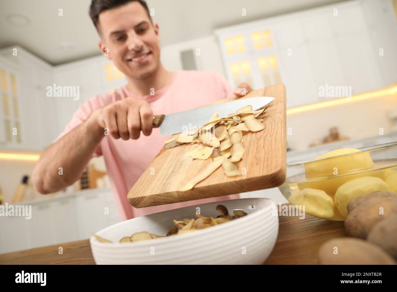 Man with cutting board and knife scraping vegetable peels into bowl in ...