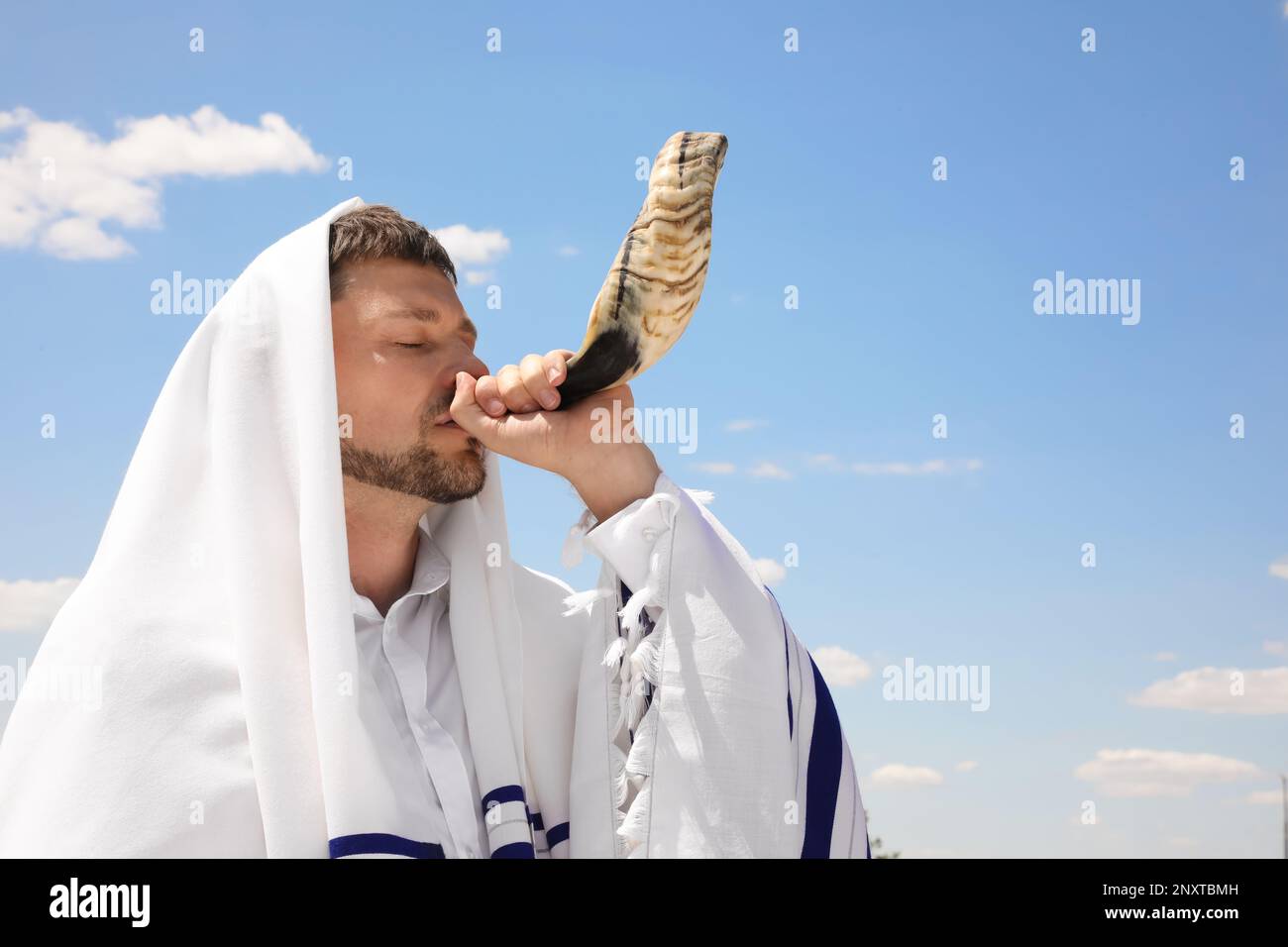 Jewish man in tallit blowing shofar outdoors. Rosh Hashanah celebration ...