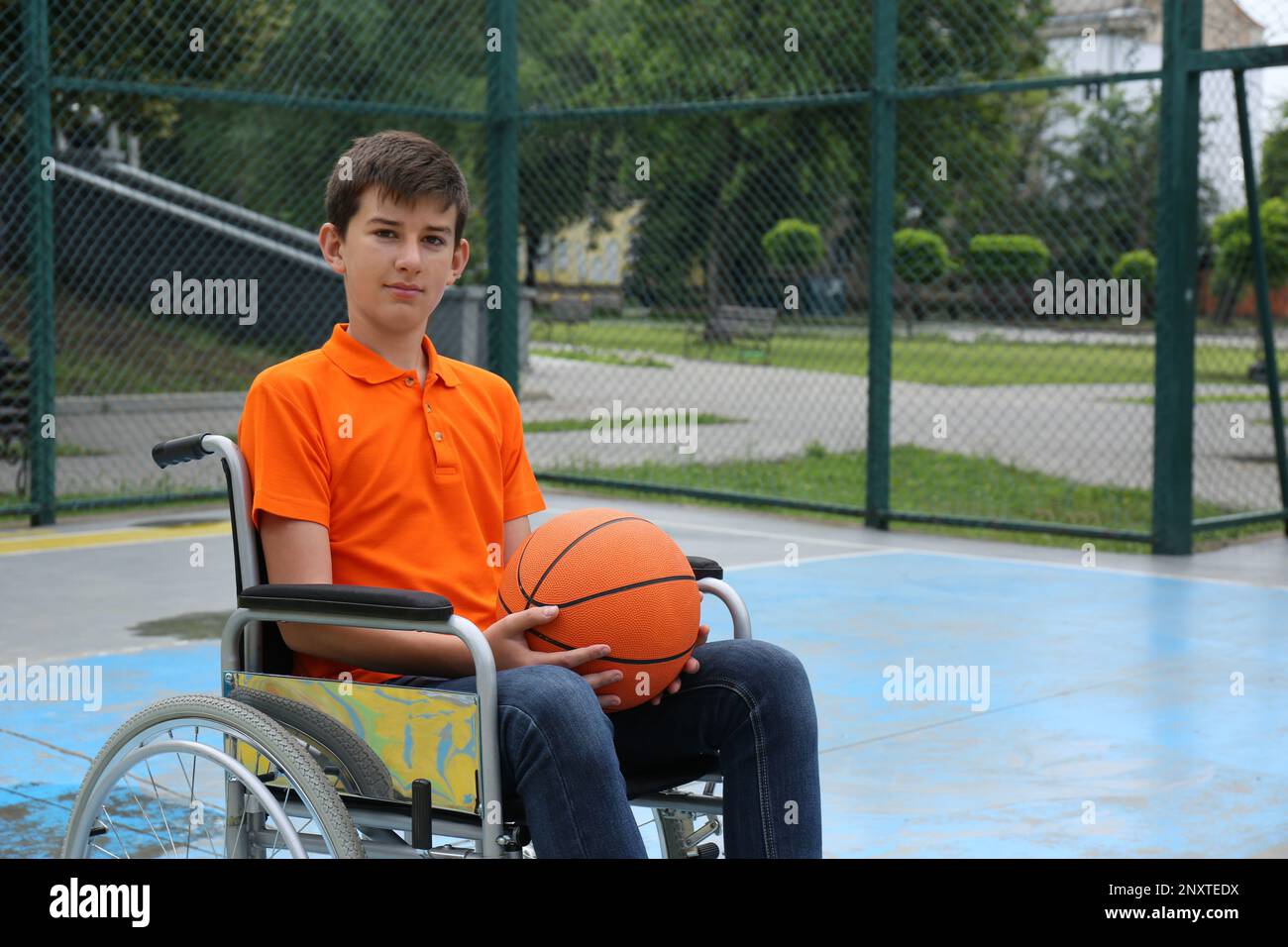 Disabled teenage boy in wheelchair with basketball ball at outdoor ...