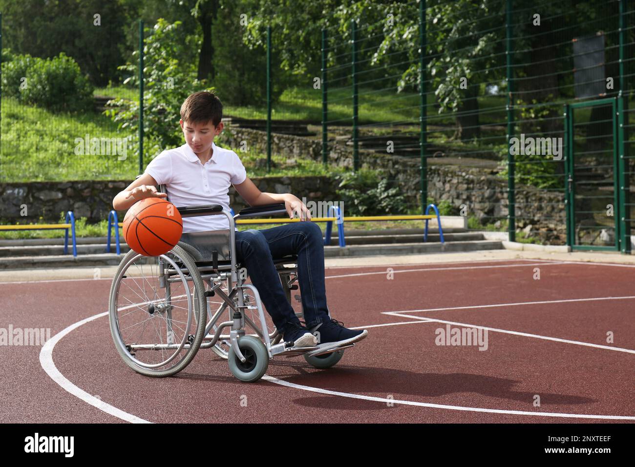Disabled teenage boy in wheelchair playing basketball on outdoor court ...