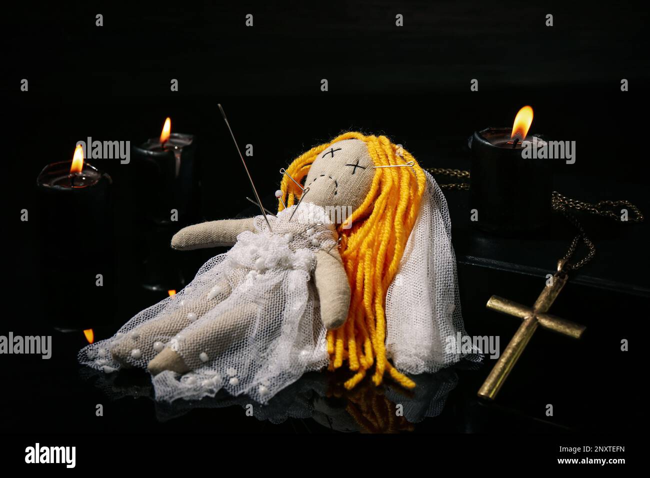 Voodoo doll pierced with pins, cross and candles on black table. Curse ...