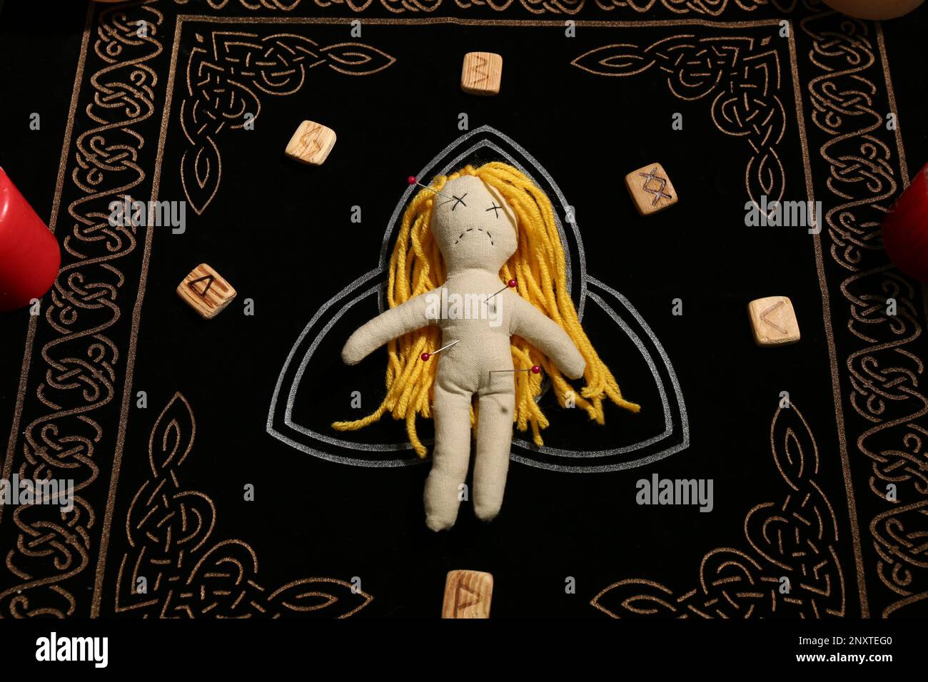 Voodoo doll pierced with pins and runes on black mat, above view. Curse ...